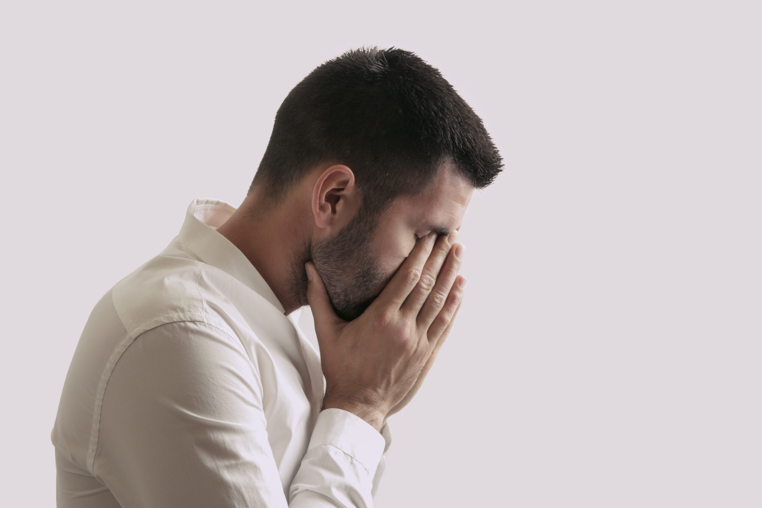 Portrait of depressed young man, covering face with his hands, side ...